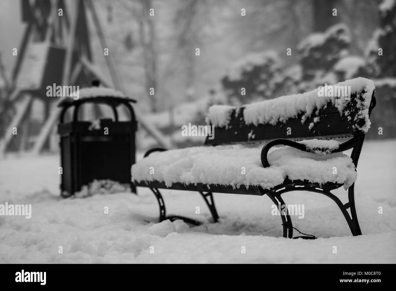 A snow-covered bench in the park. A bench covered with snow by the path ...