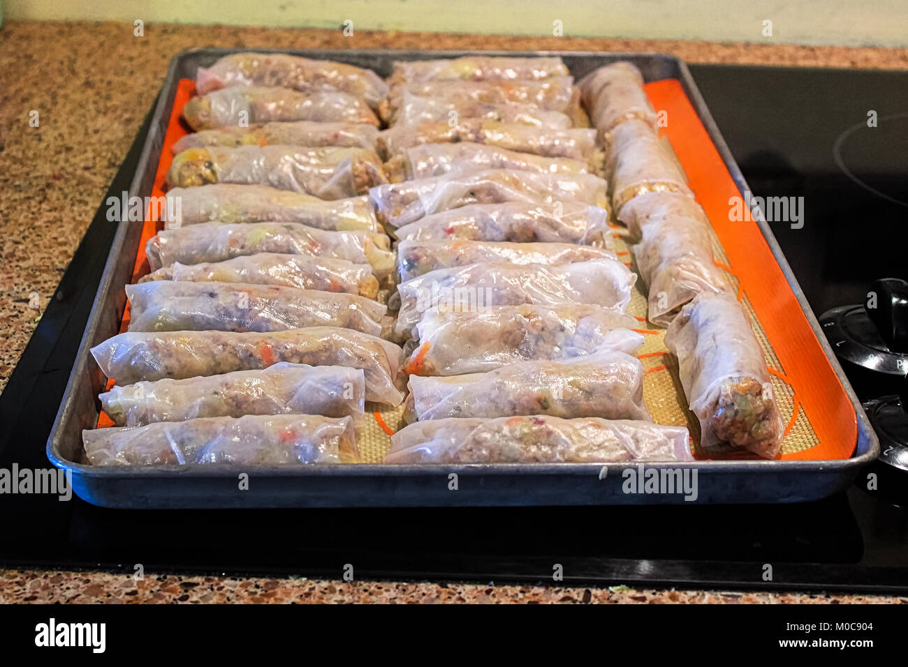 A tray of spring rolls wrapped and ready for freezing Stock Photo - Alamy