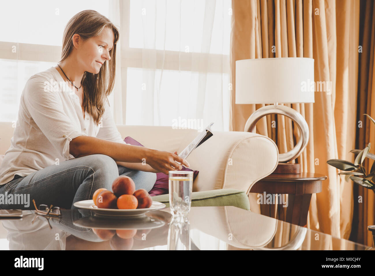 Mature woman is relaxing on a couch in her apartment with a magazine ...