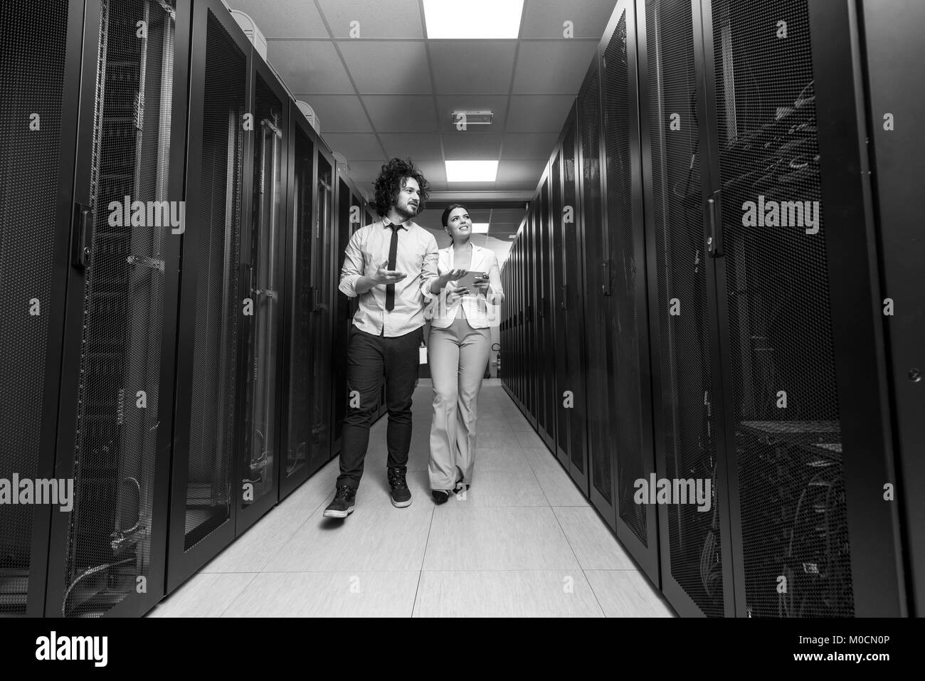 Young IT engineer showing working data center server room to female ...