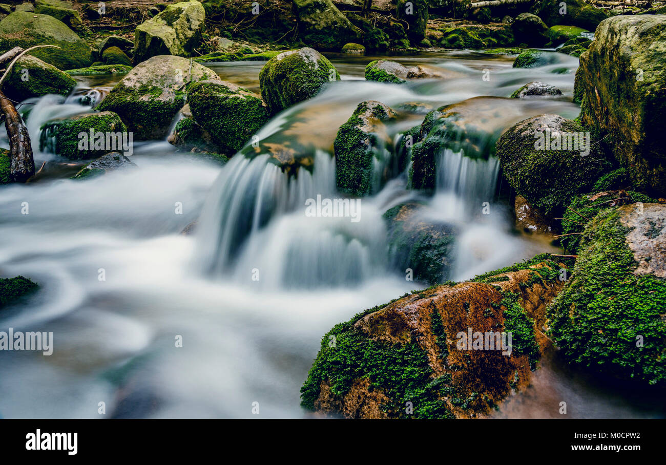 Wild natural water scenery of a small waterfall with blurred water flow ...