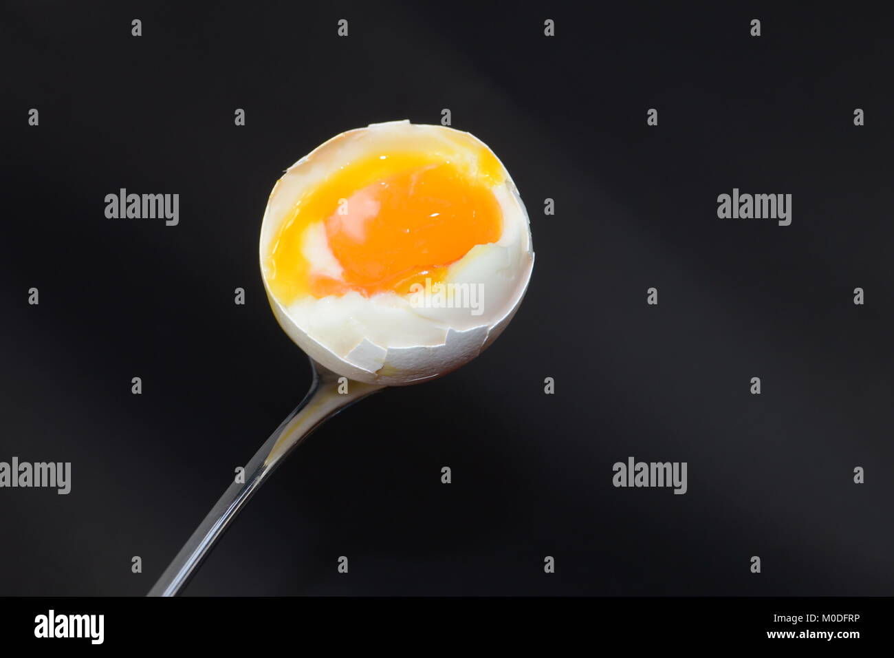 A opened, boiled egg on a silver spoon on a black background Stock ...