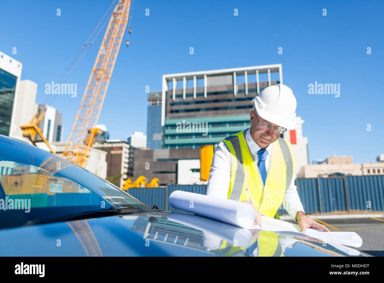 Senior foreman in glasses doing his job at building area on car hood ...