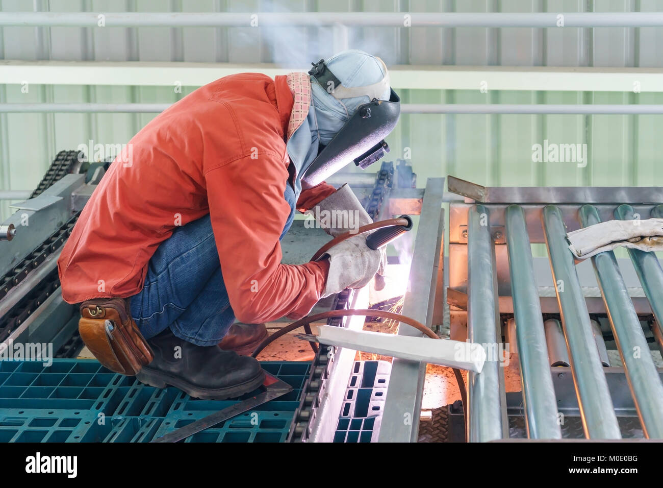 Male worker wearing protective clothing welding the steel structure ...