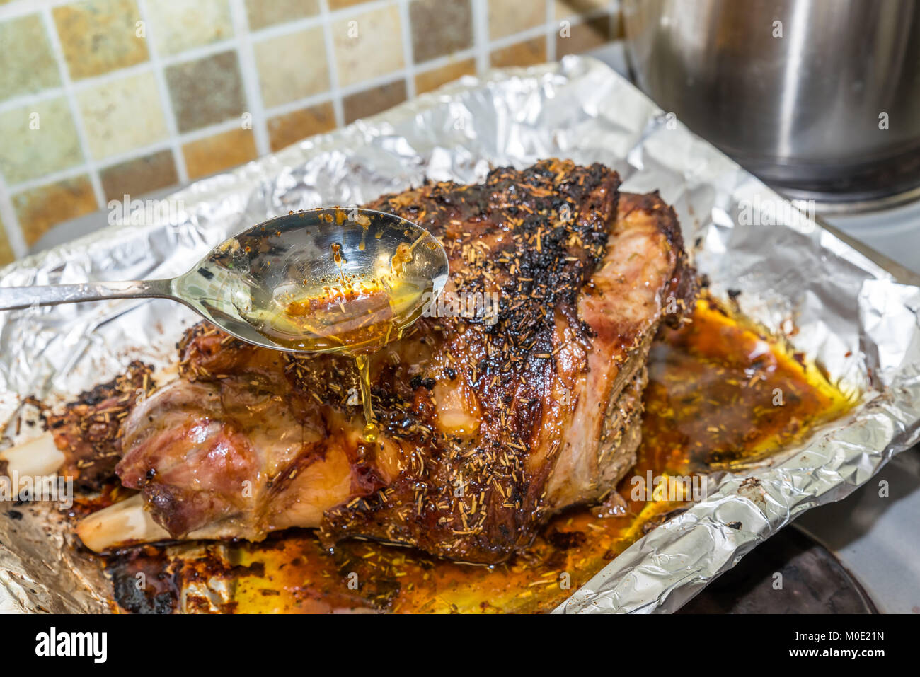 Closeup spoon with juice sauce over cooked lamb leg joint on roasting ...
