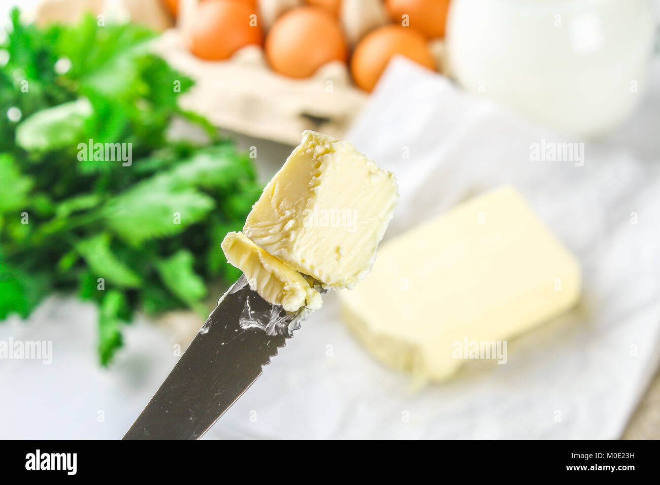 A bar of butter is cut into pieces on a wooden board with a knife ...
