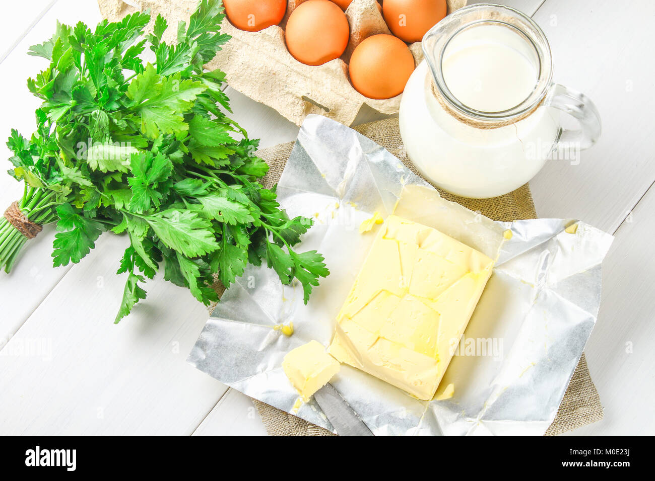 A bar of butter is cut into pieces on a wooden board with a knife ...