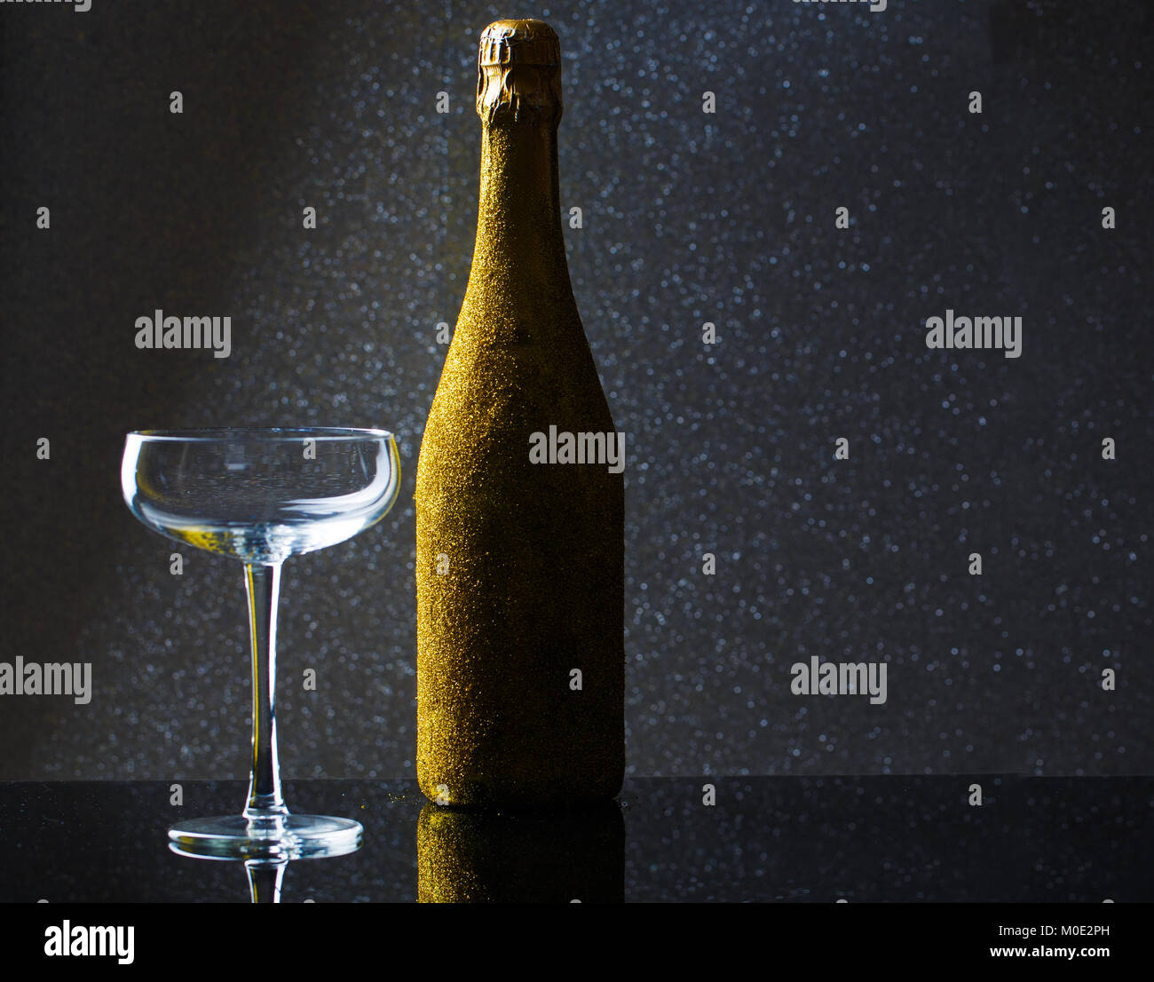 Photo of bottle of champagne in gold wrapper with empty wine glass ...