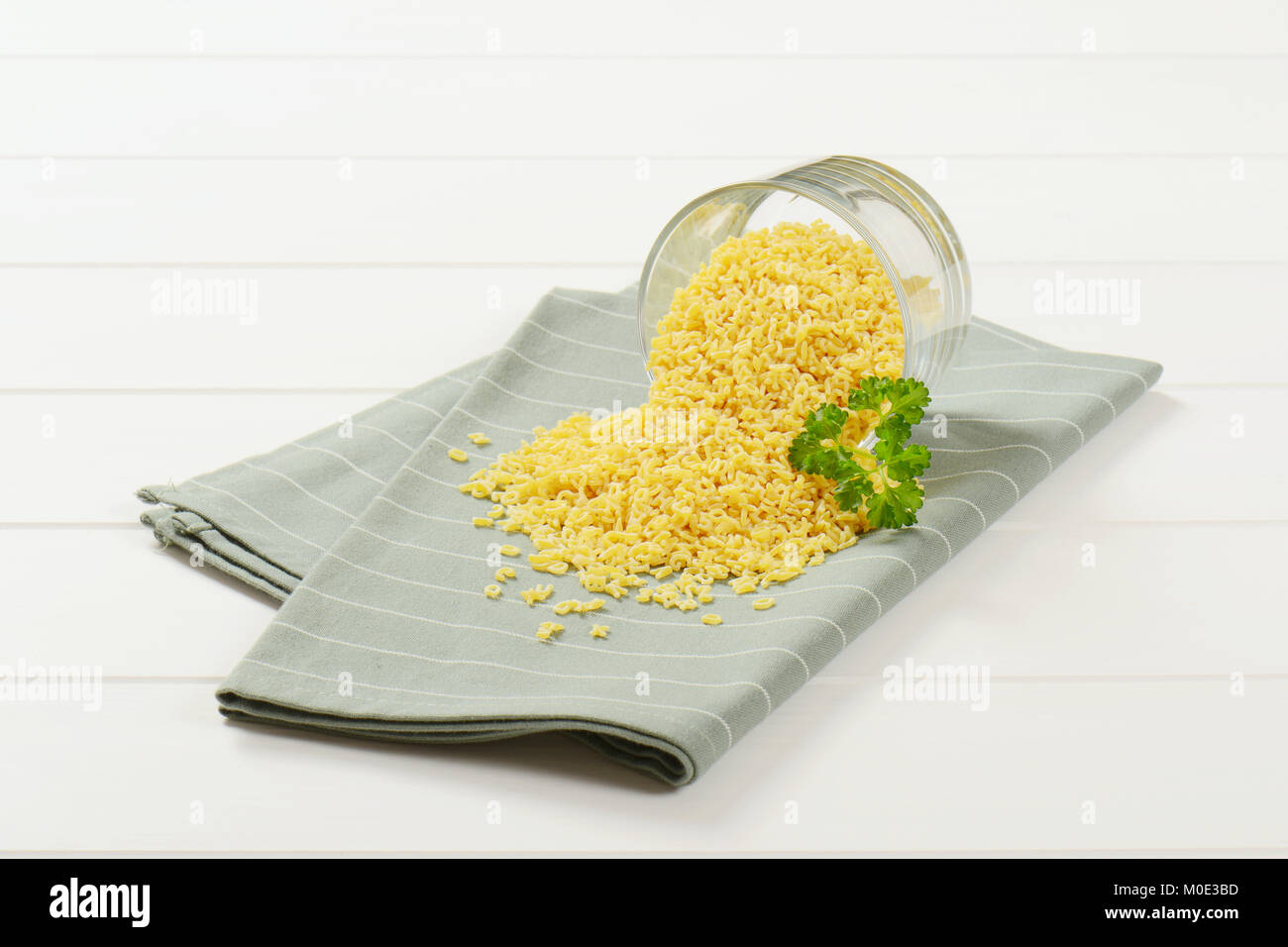 glass of uncooked alphabet pasta spilt out on grey place mat Stock ...