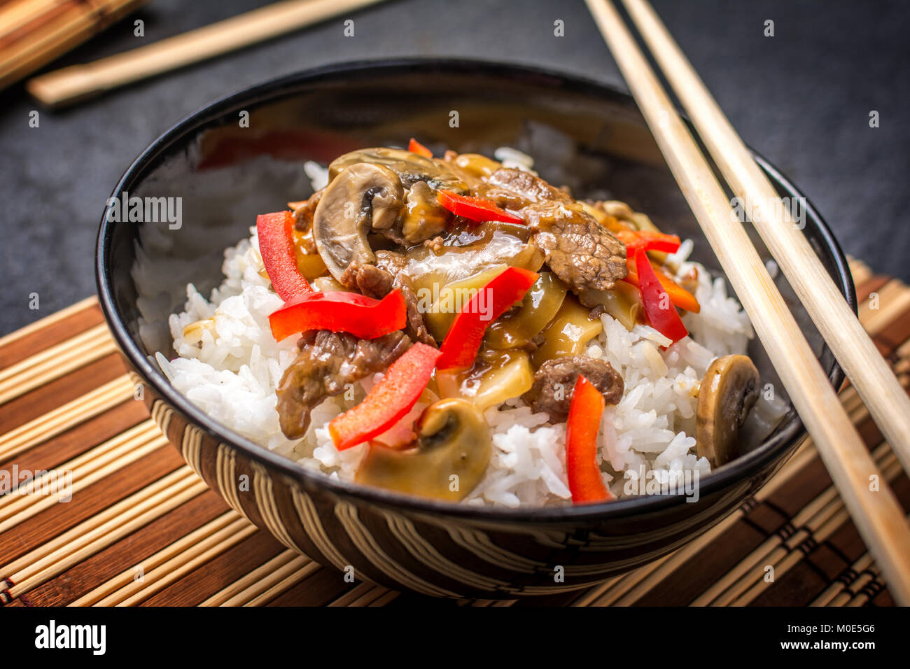 Asian rice with beef in black plate with chopsticks on dark stone table ...