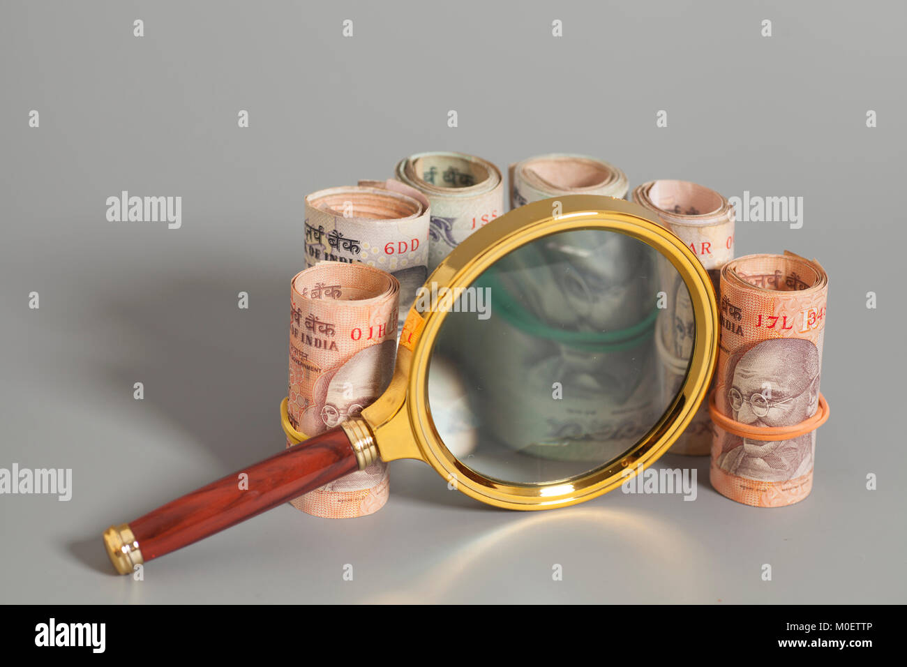 Rolls of Indian Currency Rupee Notes with magnifying glass on gray ...