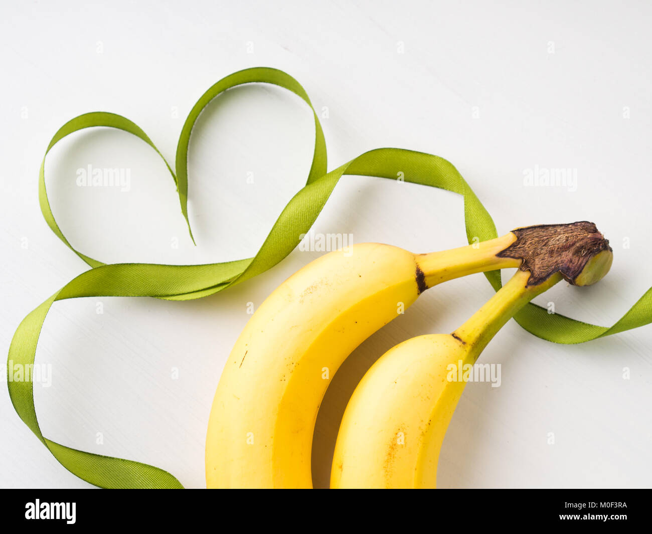 Two bananas with green ribbon frame and heart symbol on white ...