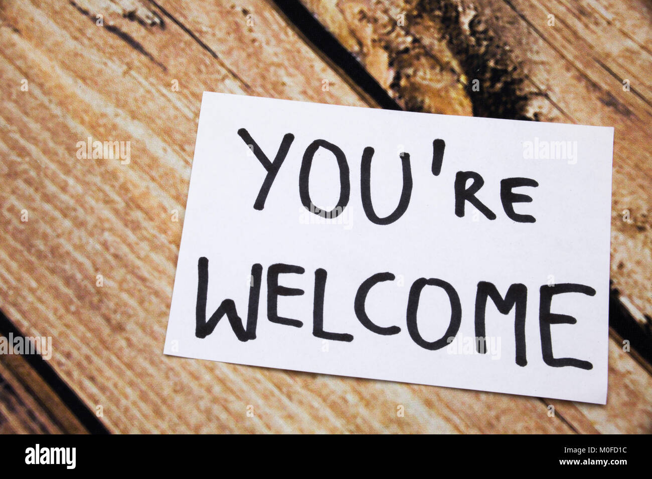 You are welcome handwriting in a black ink sticky note on wooden table ...