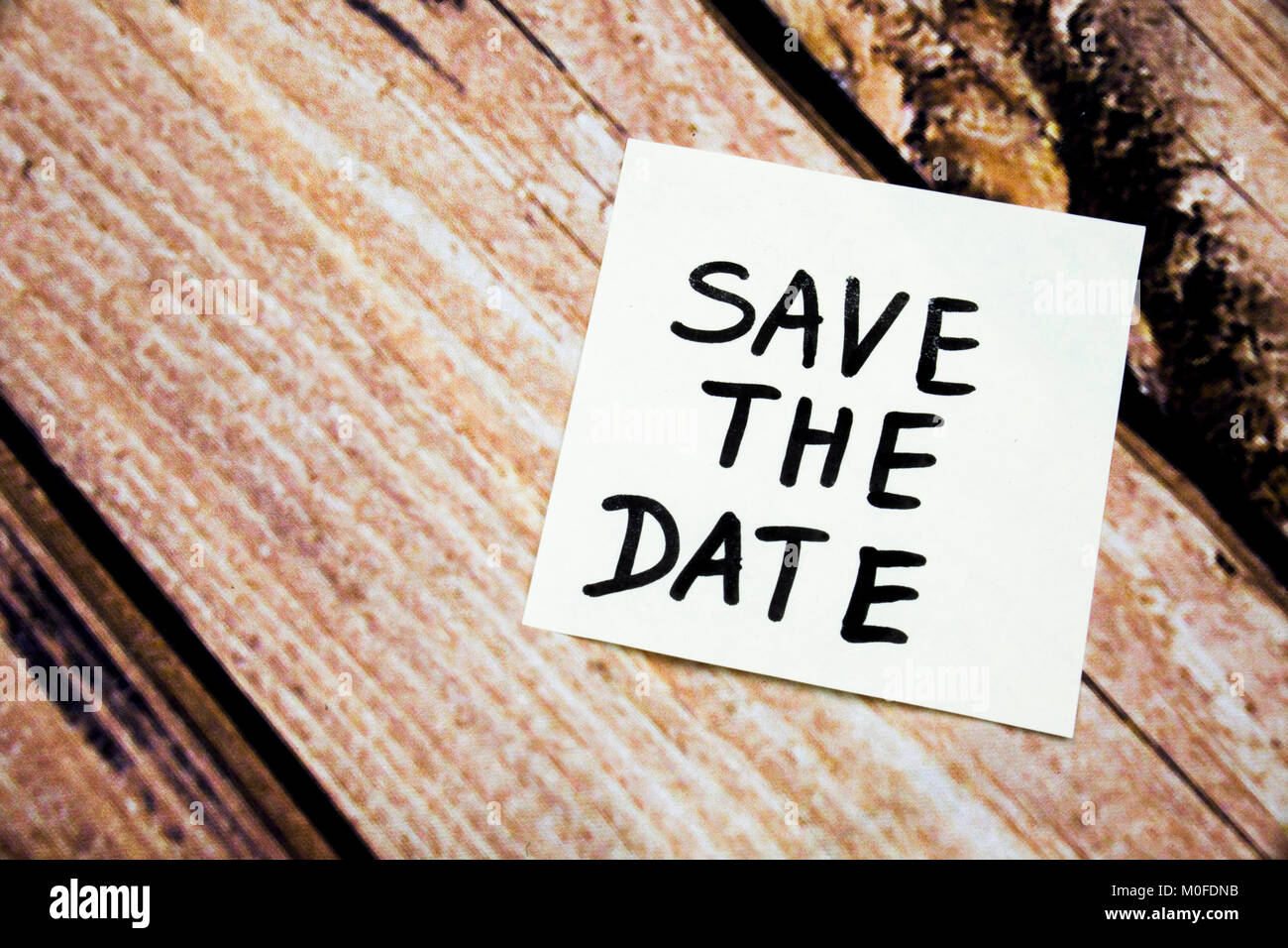 sticky note on the wooden background with the phrase save the date ...