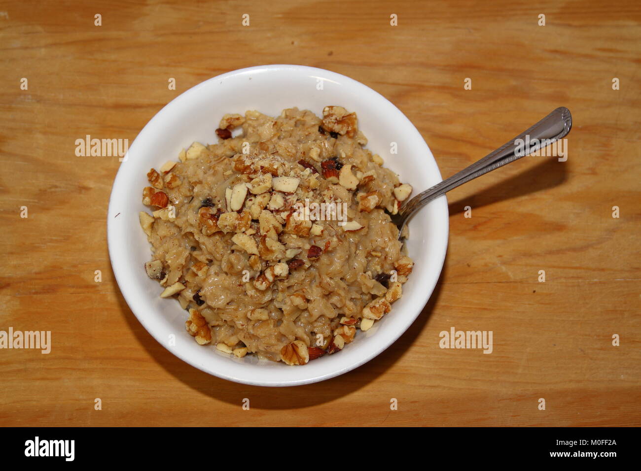 Oatmeal with raisins and chopped nuts in a white bowl on a wooden ...