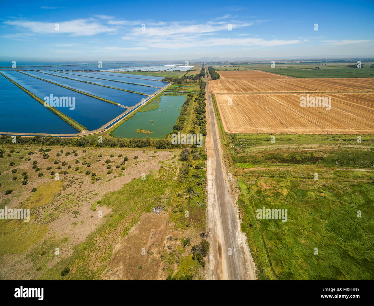 Straight unsealed road passing between plowed field and water treatment ...
