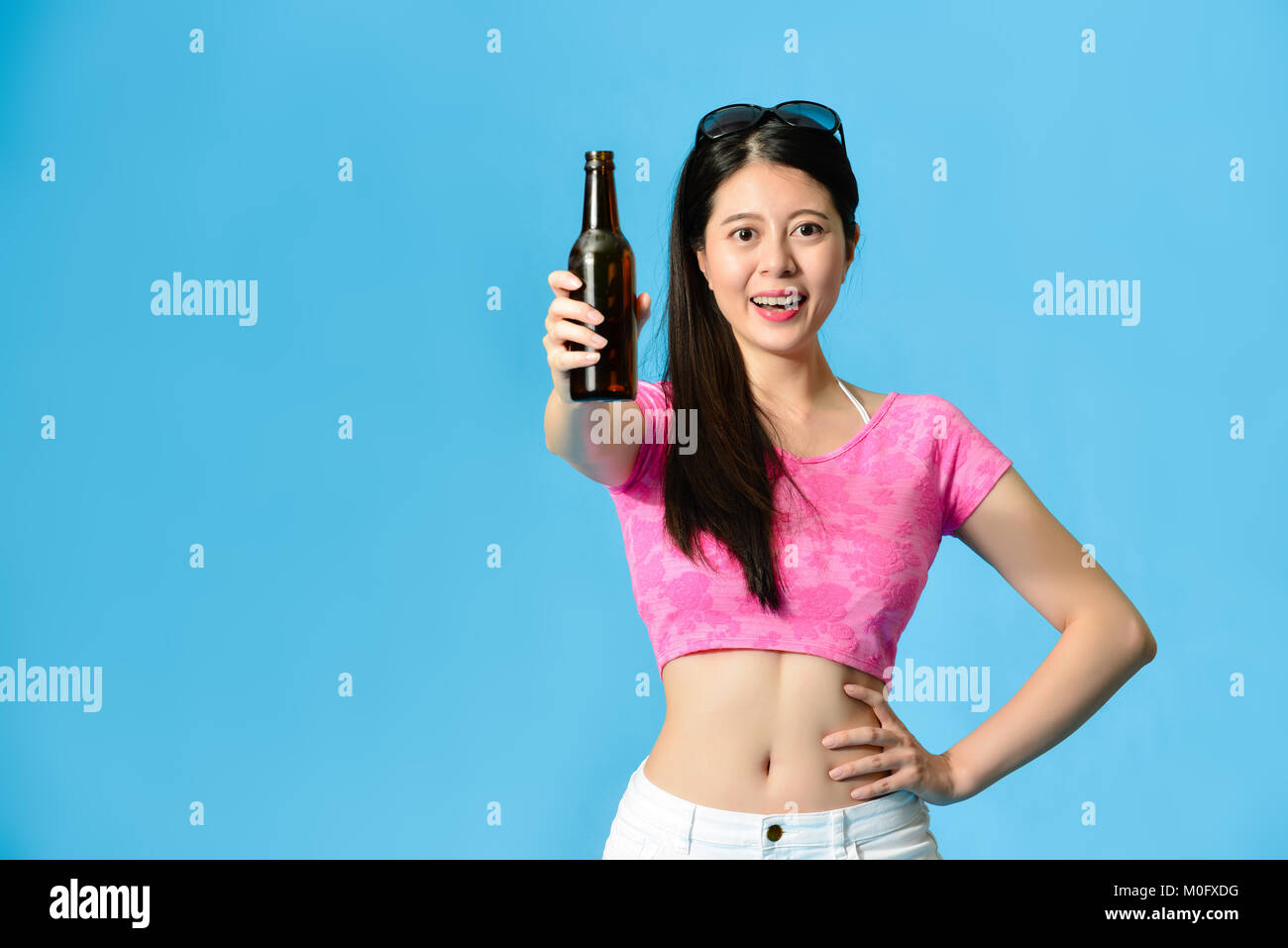smiling beauty girl face to camera showing beer bottle isolated on blue ...