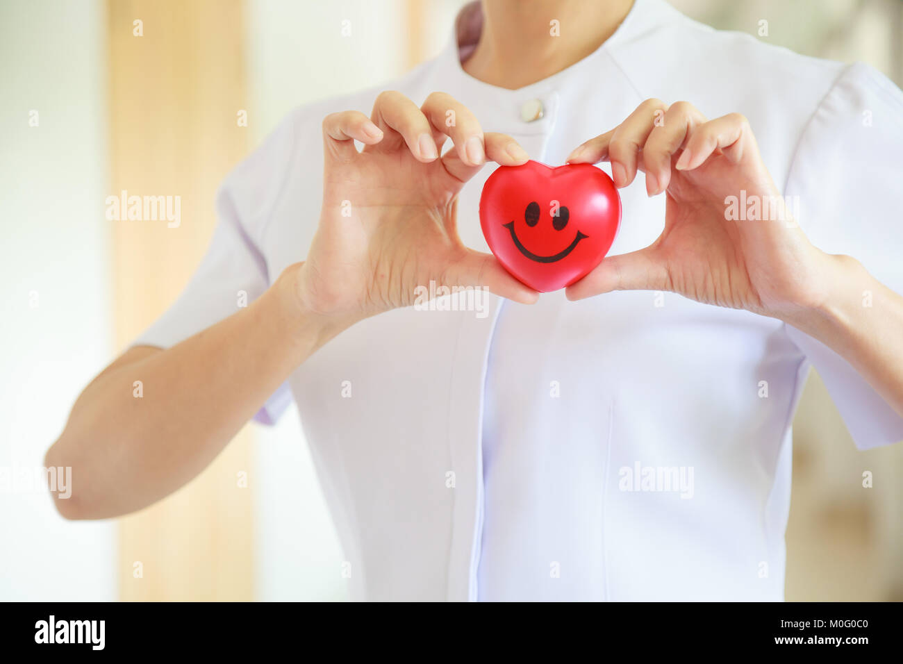 Red smiling heart held by female nurse's both hands, representing ...