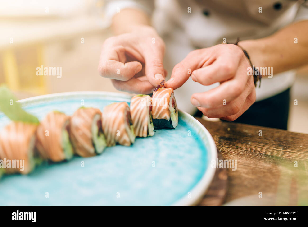 Male person cooking sushi rolls with salmon on wooden table, japanese ...