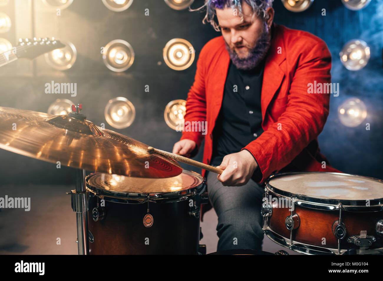 Bearded drummer in red suit, performing on the stage with lights, retro ...
