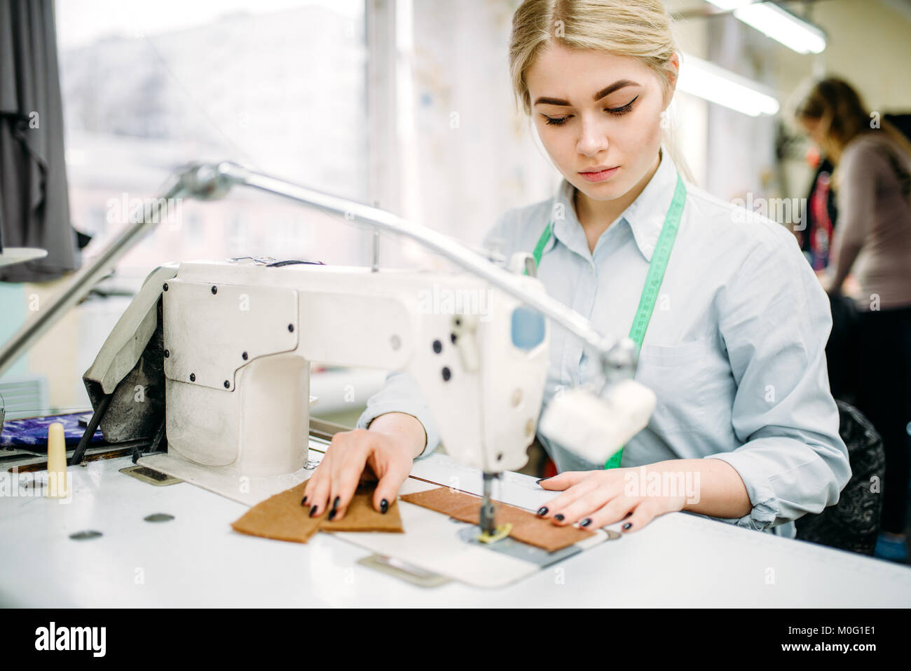 Needlewoman sews fabrics on a sewing machine. Tailoring or dressmaking ...