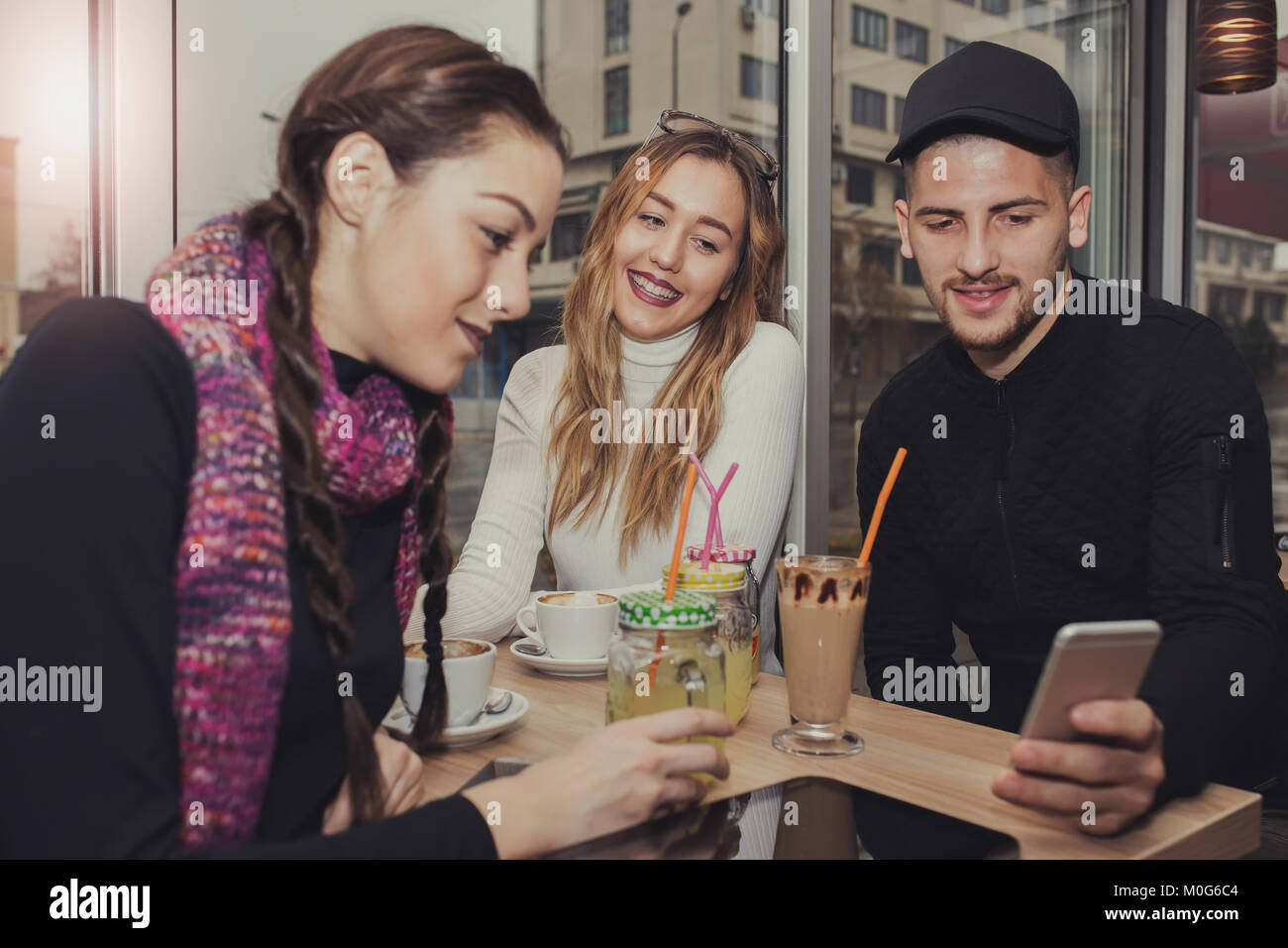 Cheerful group of friends, one man and two women sitting at the table ...