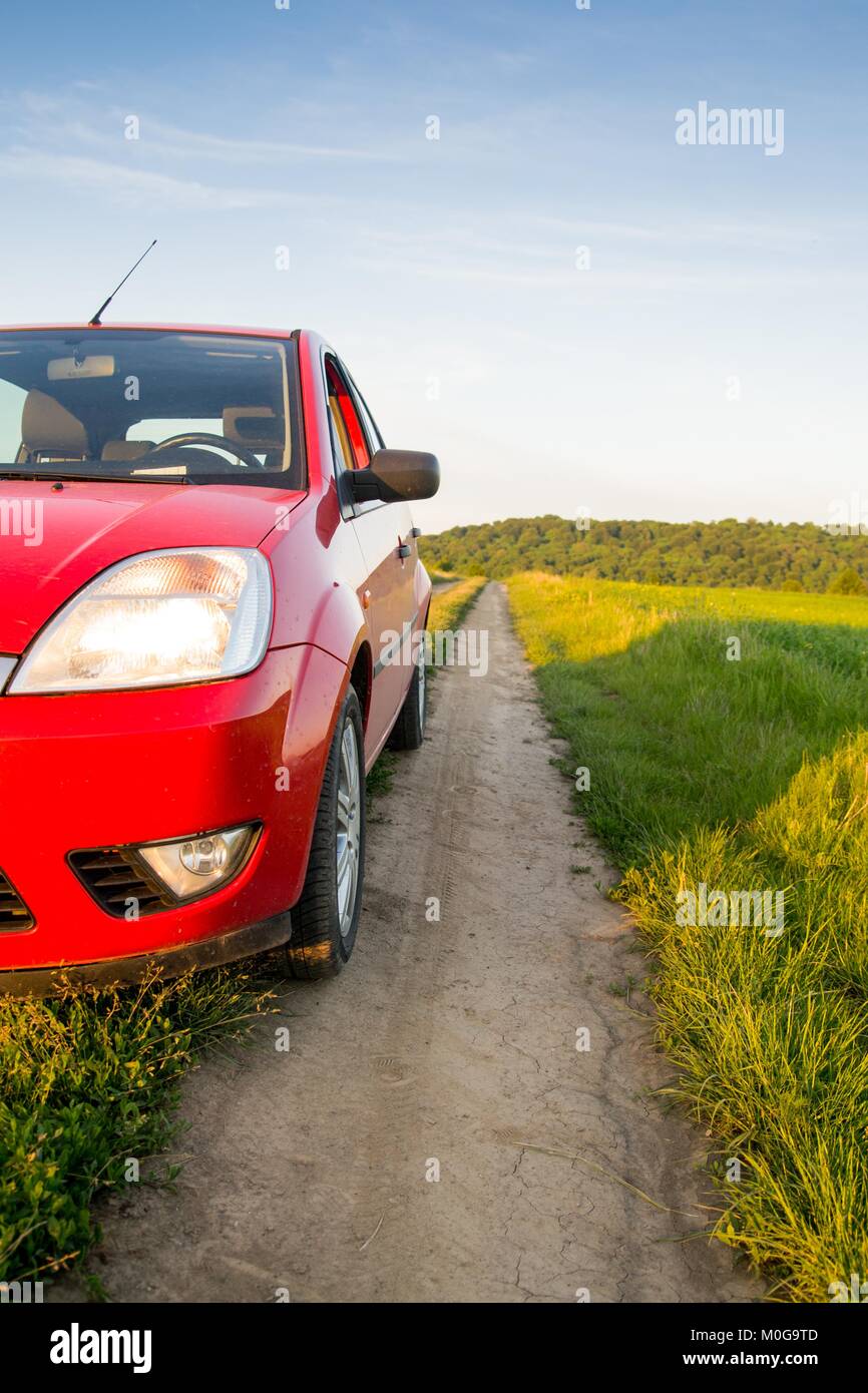 One side of a red car on a country road near a green field Stock Photo ...
