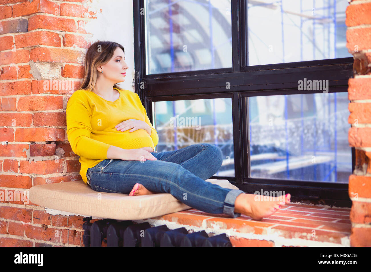 Pretty pregnant woman indoors sitting near window Stock Photo - Alamy