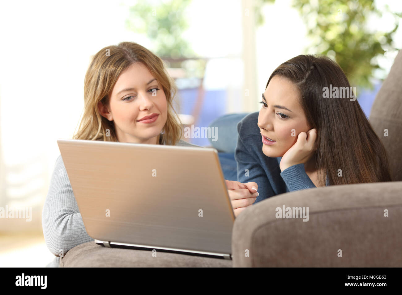 Portrait of two friends talking about online content in a laptop lying ...