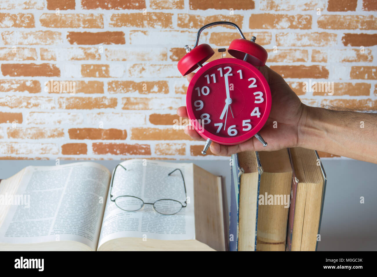 A man holding alarm clock above open books , reading time Stock Photo ...