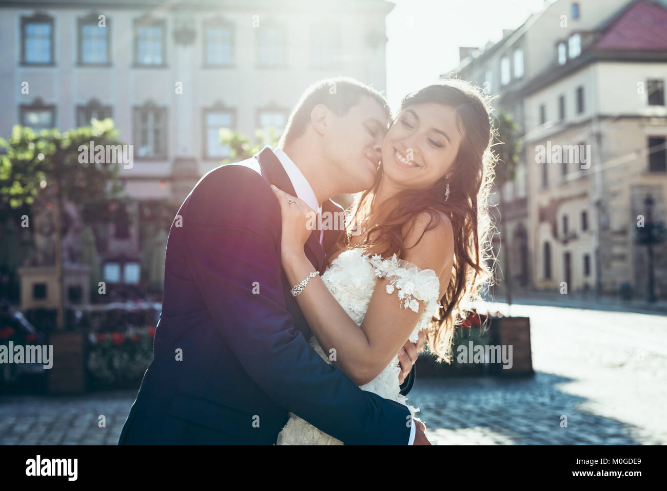Wedding portrait in the sun of the handsome groom kissing the beautiful ...
