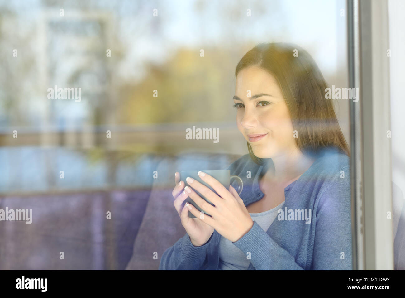 Serious woman looking forward through a window at home with outside ...