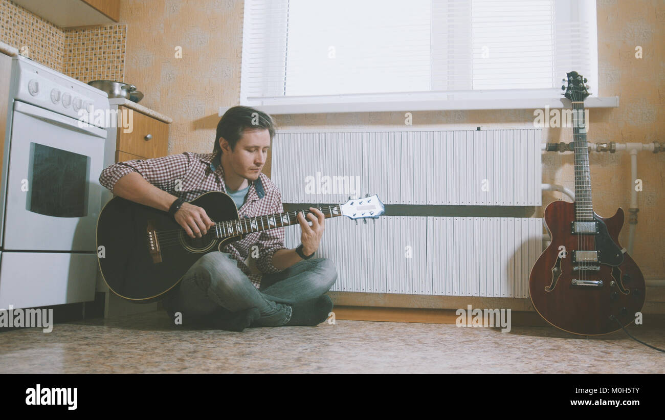 Young man composes music on the guitar and plays in the kitchen, other ...