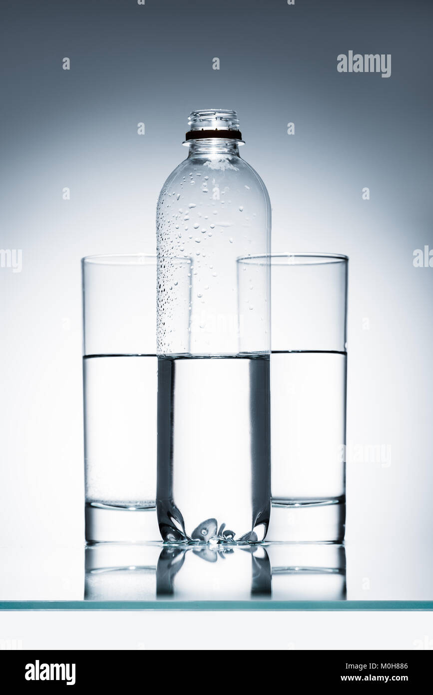 plastic bottle and glasses of clean water on reflective surface Stock ...