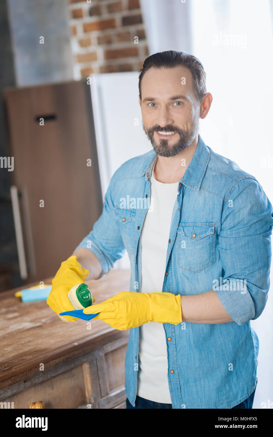 Cheerful male cleaner using cleanser Stock Photo - Alamy