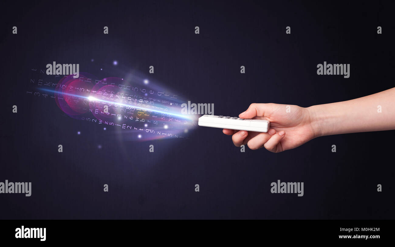 Hand holding a remote control, shining numbers and letters coming out ...