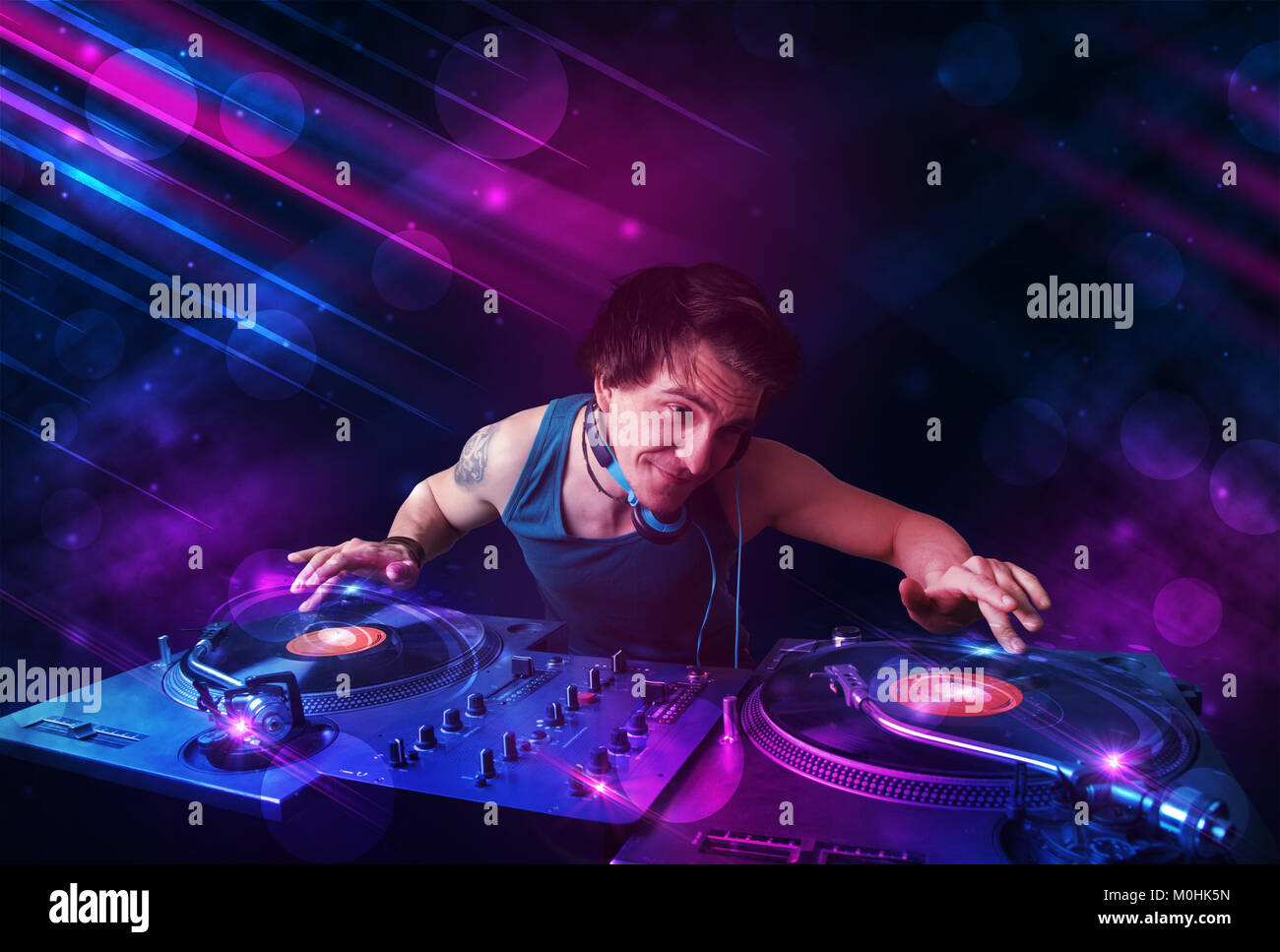 Attractive young DJ playing on turntables with color light effects ...