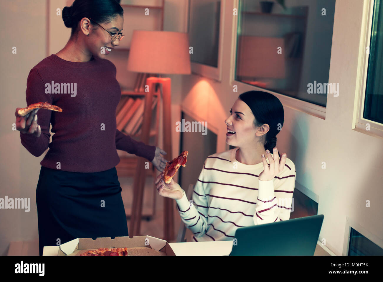 Cheerful friends talking to each other while eating pizza Stock Photo ...