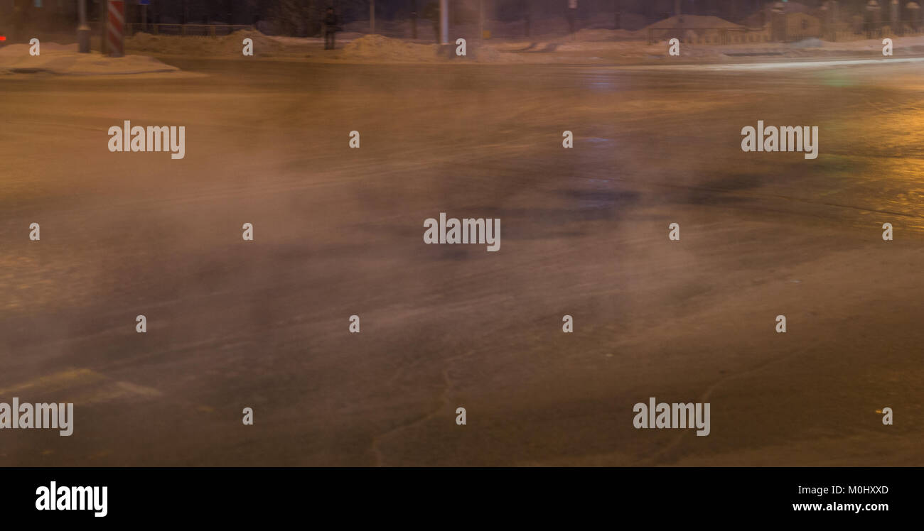 steam on the road, winter evening city asphalt vapor from the cold ...