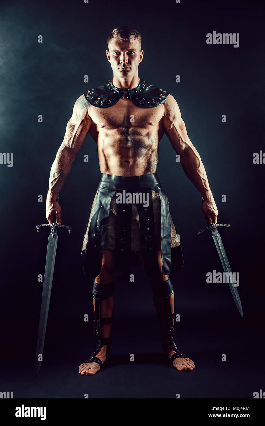 Portrait of handsome muscular gladiator with two swords. Studio shot ...