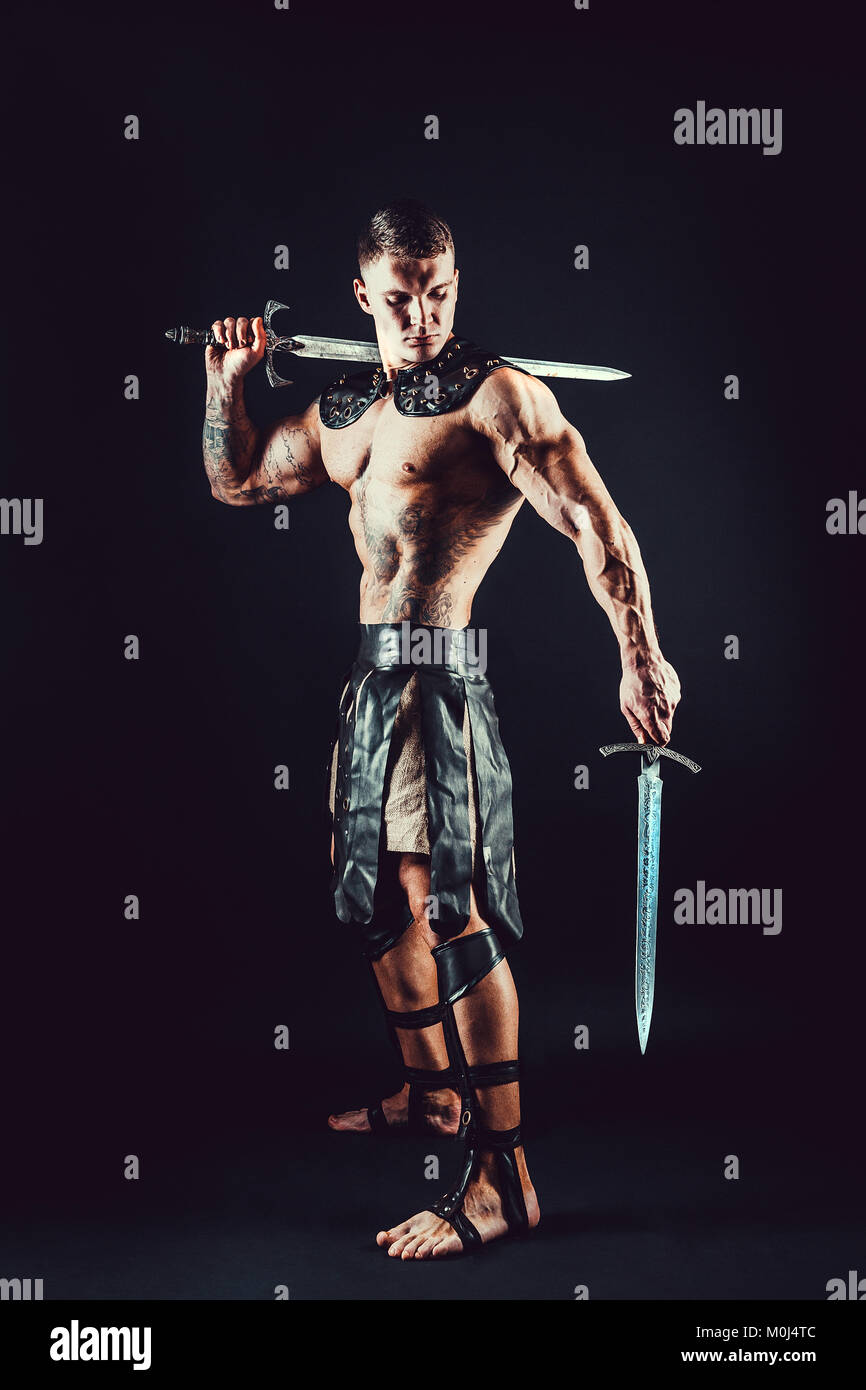 Portrait of handsome muscular gladiator with two swords. Studio shot ...