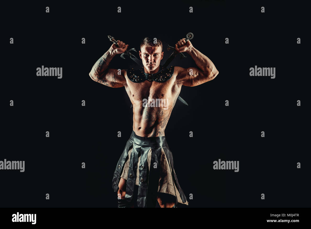 Portrait of handsome muscular gladiator with two swords. Studio shot ...