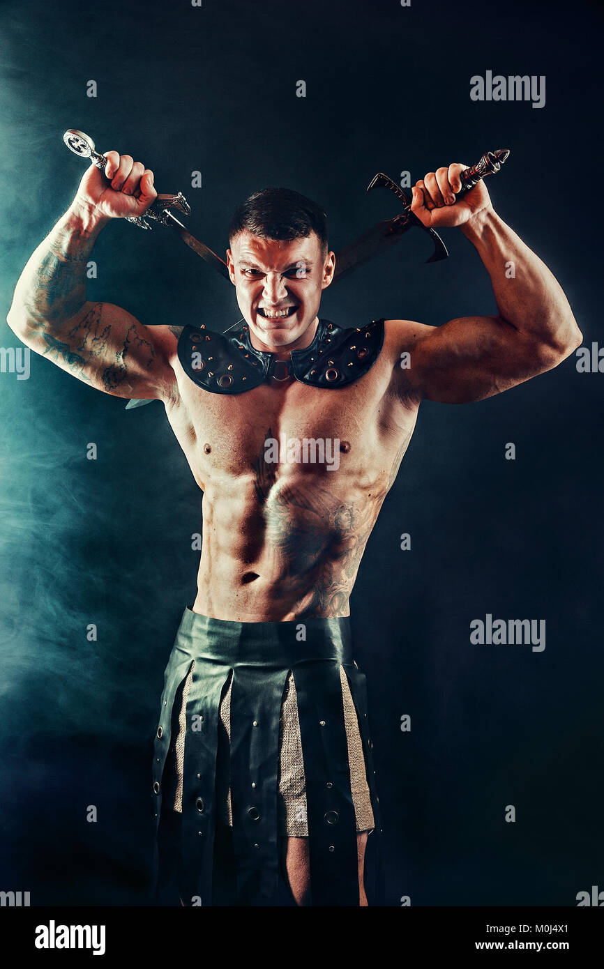 Portrait of handsome muscular gladiator with two swords. Studio shot ...