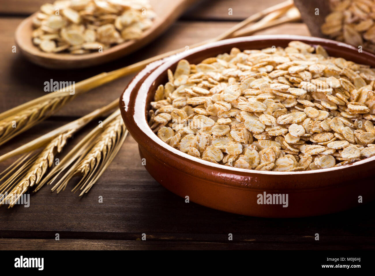 Oat flakes, uncooked oats in bowl with wooden spoon and wheat ears ...