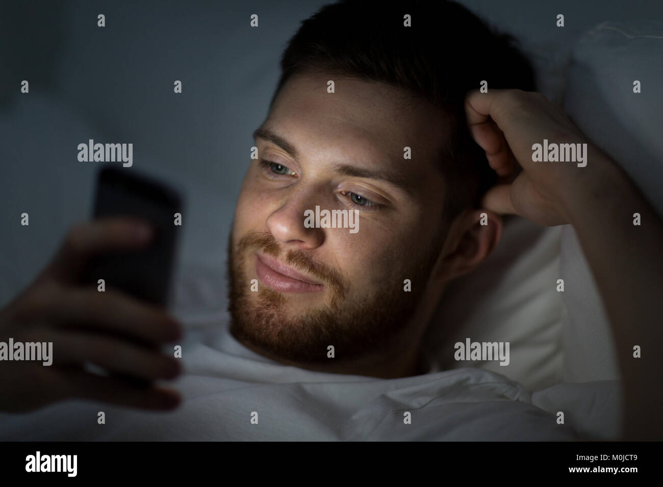 happy young man with smartphone in bed at night Stock Photo - Alamy