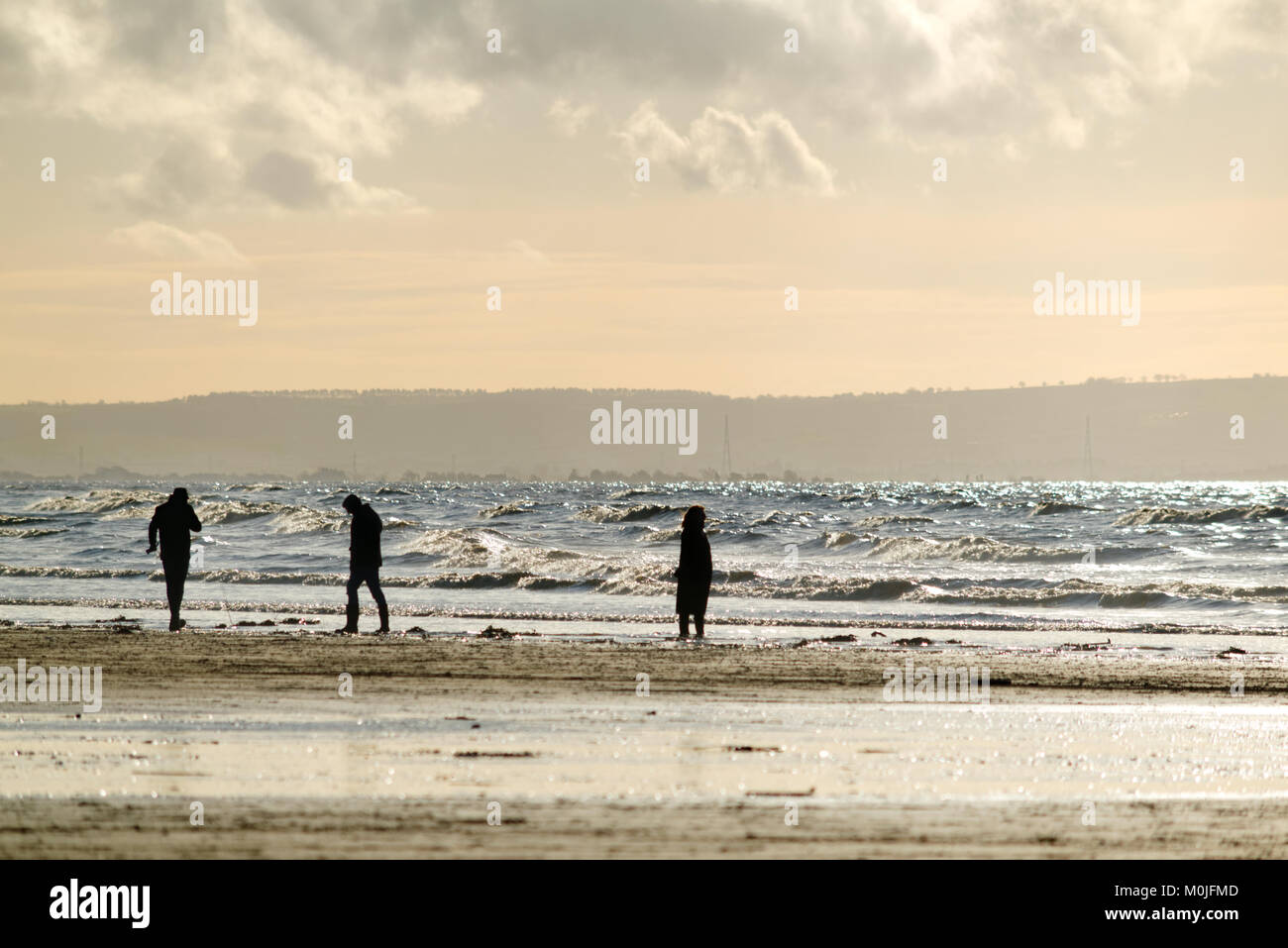 Silhouette of three people walking on Brean beach looking out to sea ...