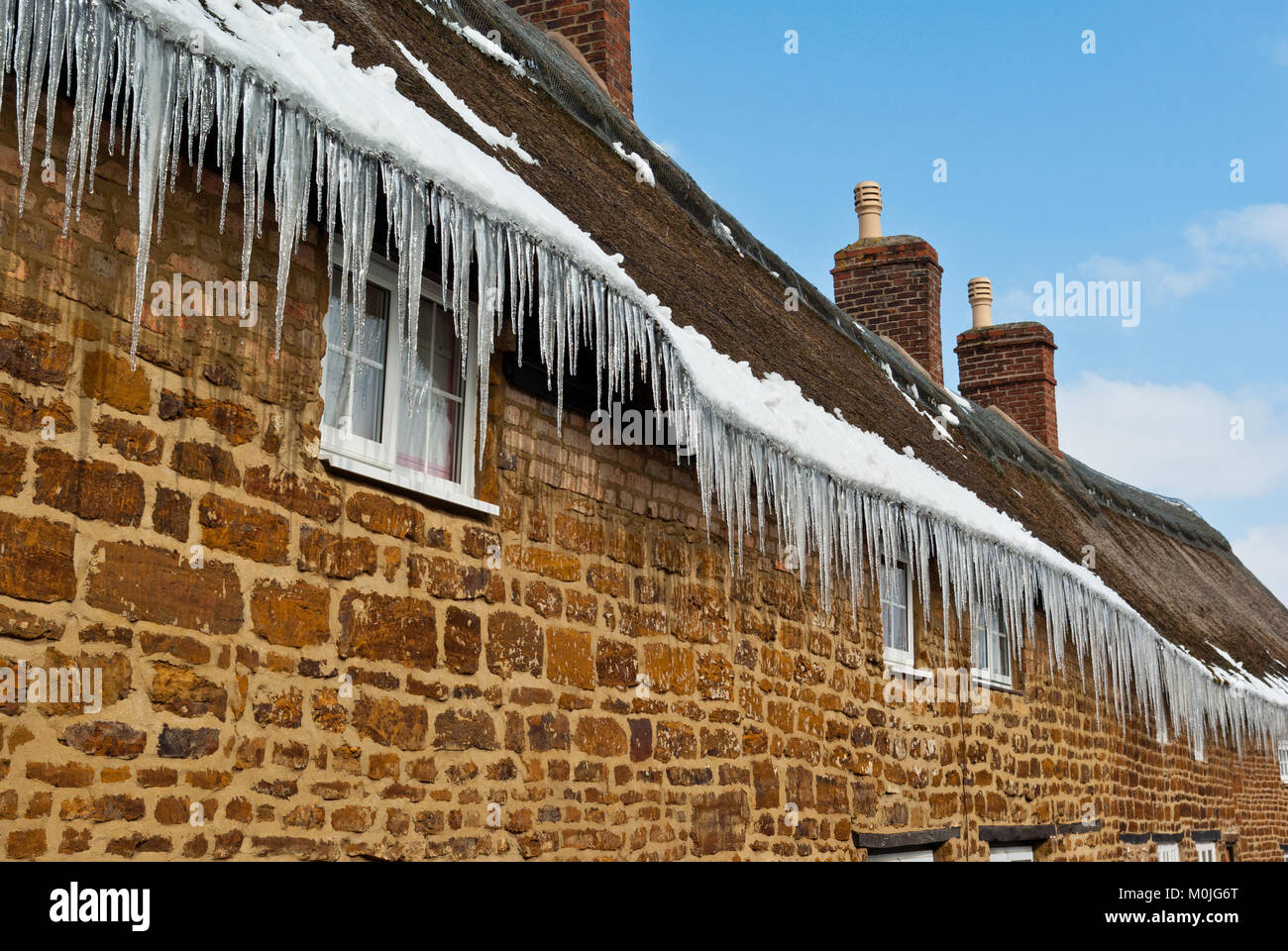 Long line of icicles hanging from the thatched roof of a stone cottage ...