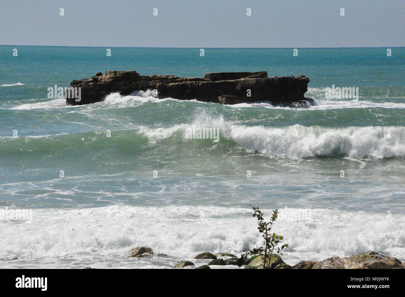 A rock stands steadfast in the middle of the sea as waves crash on the ...