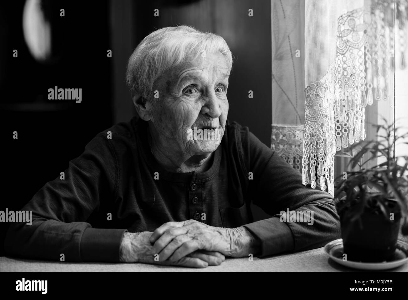 Elderly woman talking sitting at the table in the house. Black and ...