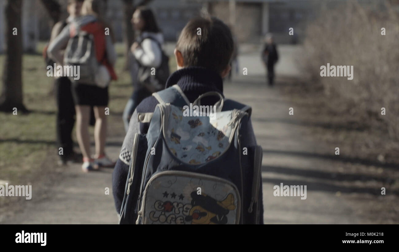Rear side view of child carrying backpack going to or from school on ...